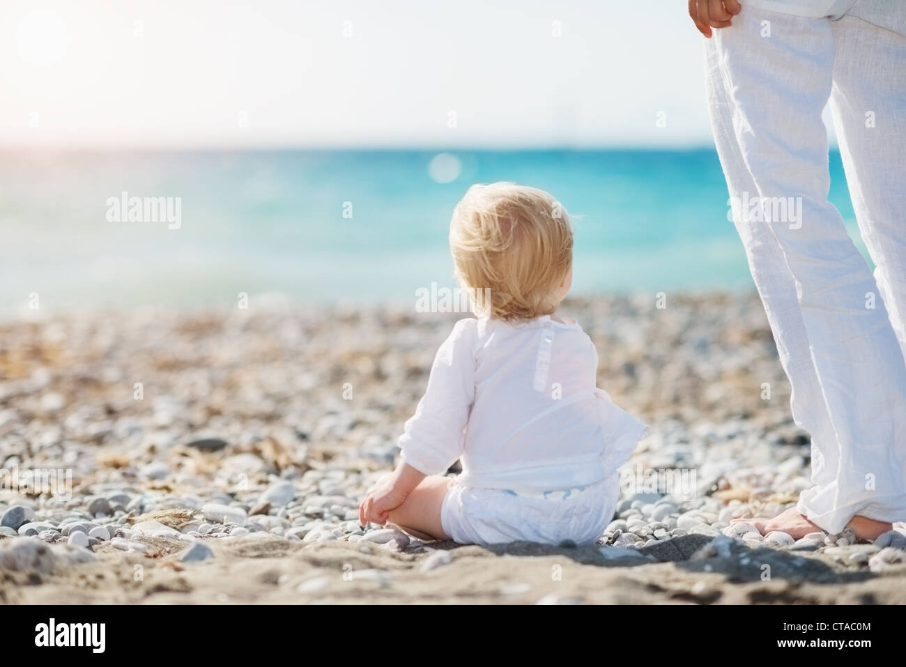 Baby sitting near mother on beach. Rear view Stock Photo - Alamy