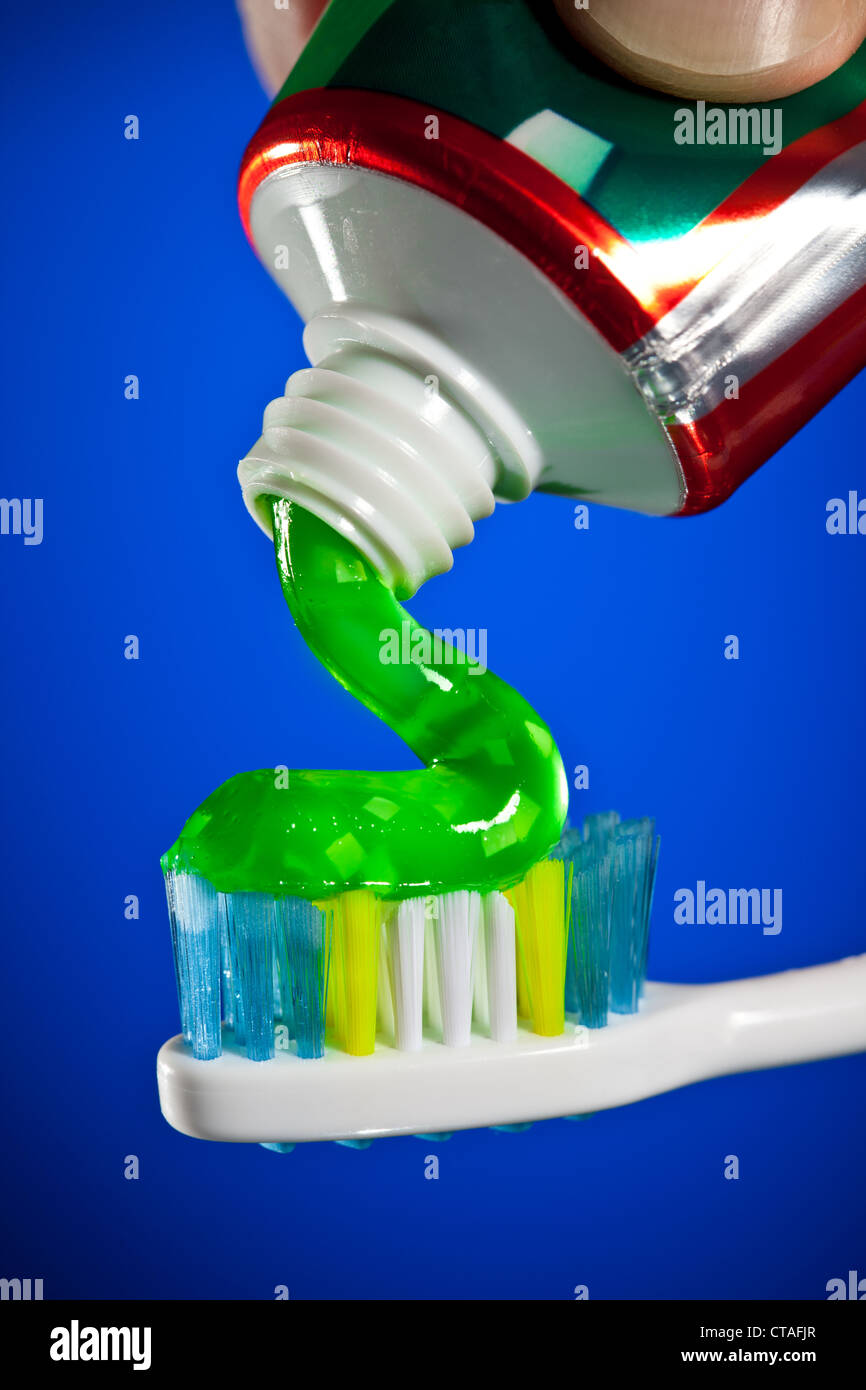 toothpaste being squeezed onto a toothbrush on a dark blue background ...