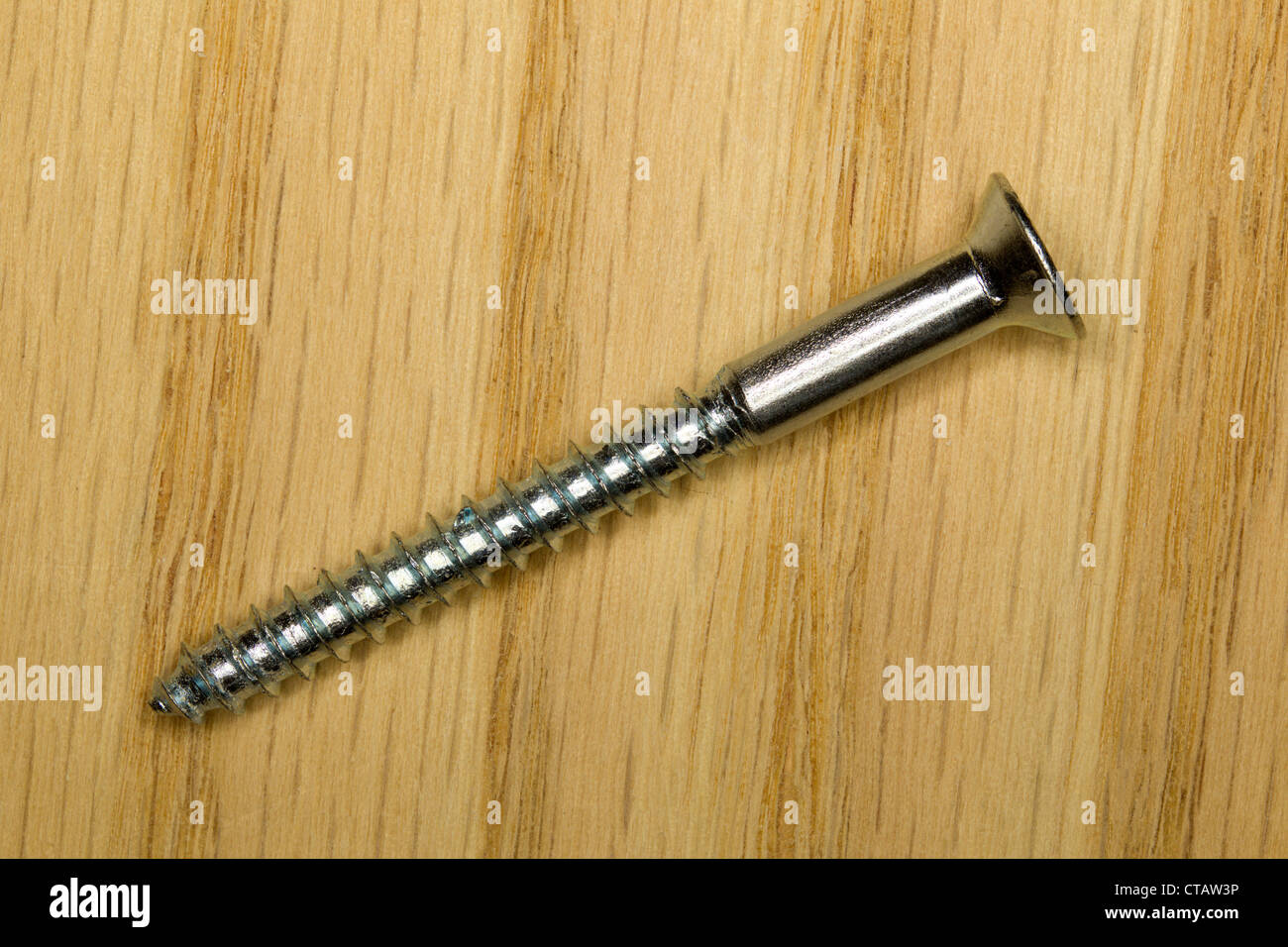 Side view of a silver steel screw laying on a piece of timber in macro ...