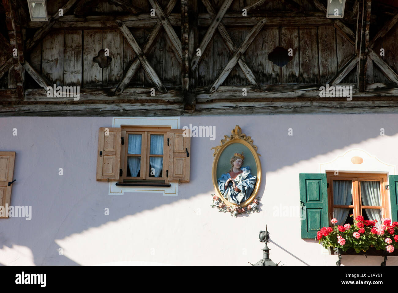 Traditional exterior wall with geraniums and depiction of a holy person ...