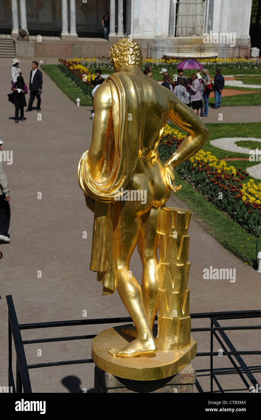 Back view of gilded statue of man looking down at gardens in Peterhof ...