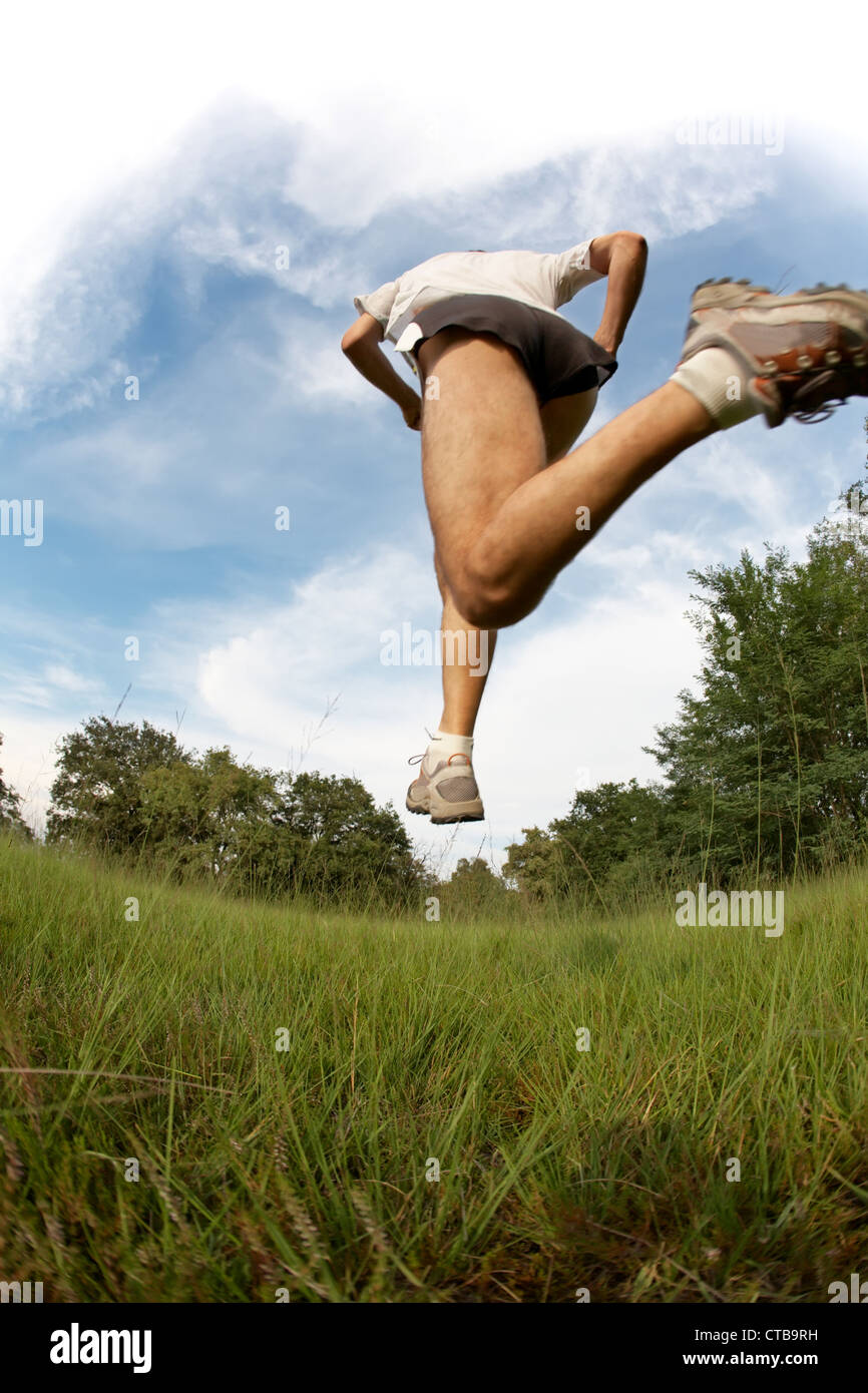 Male runner jumping and running on meadow against blue sky and clouds ...