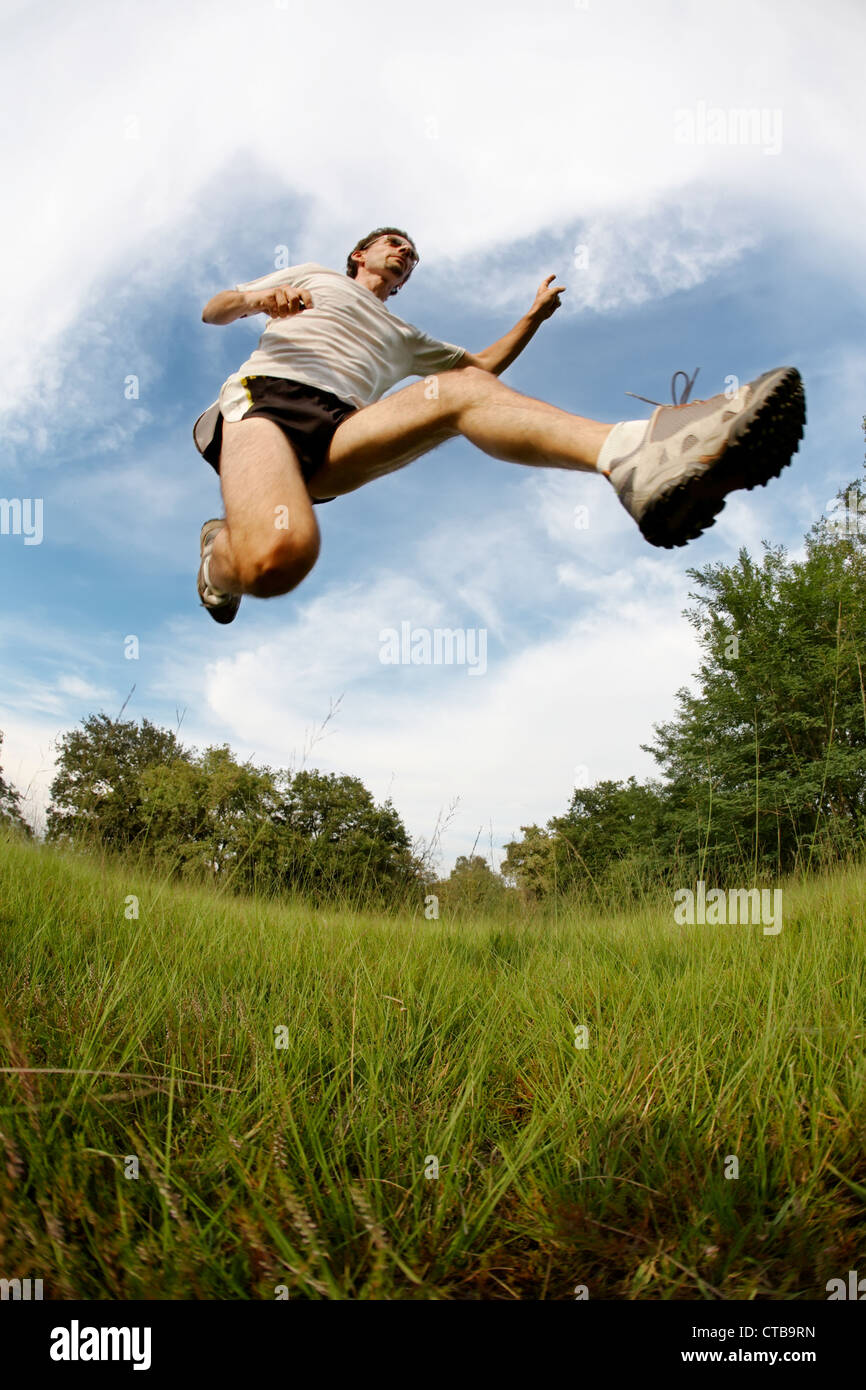 Male runner jumping and running on meadow against blue sky and clouds ...
