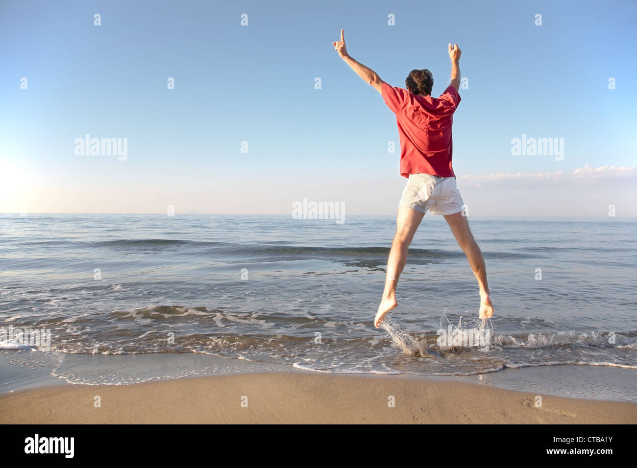 Back view of young man jumping on the beach: happiness and energy ...