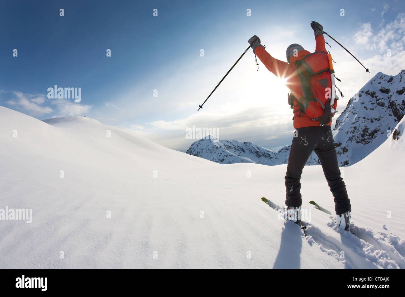 Young skier reaches his arms up over a snowy mountain landscape ...