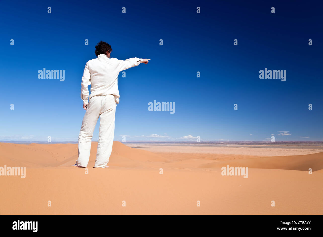 Rear view of an adult caucasian man standing on a sand dune pointing to ...