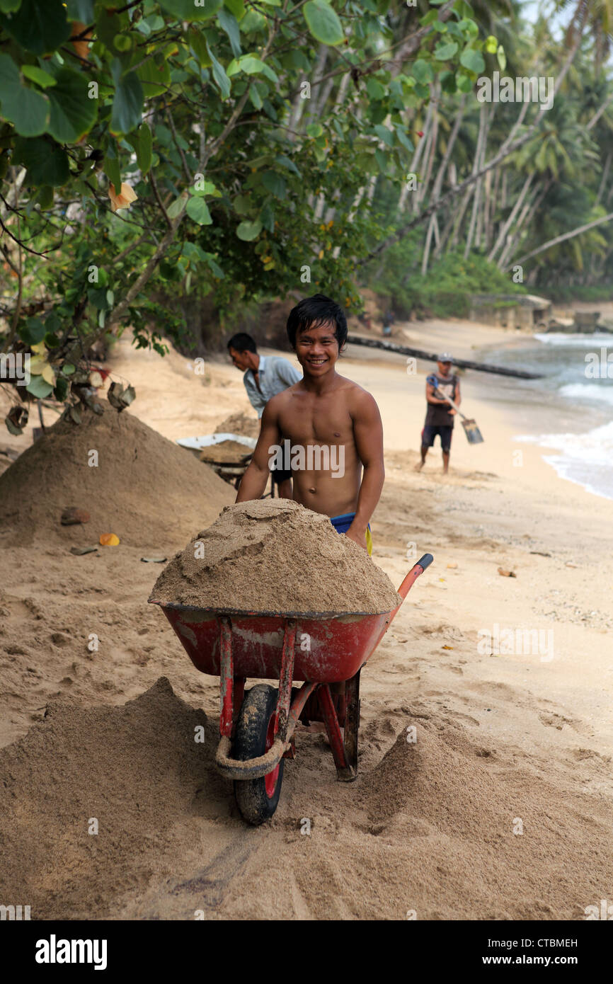 A man pushes a wheelbarrow of sand off the beach in Lagundri Bay, Nias ...