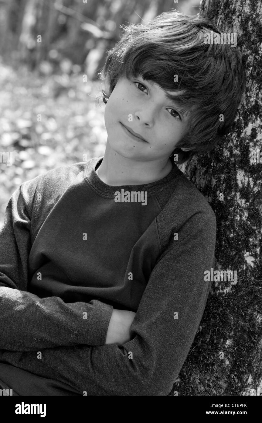 Black and white portrait of a young boy leaning against a tree in ...