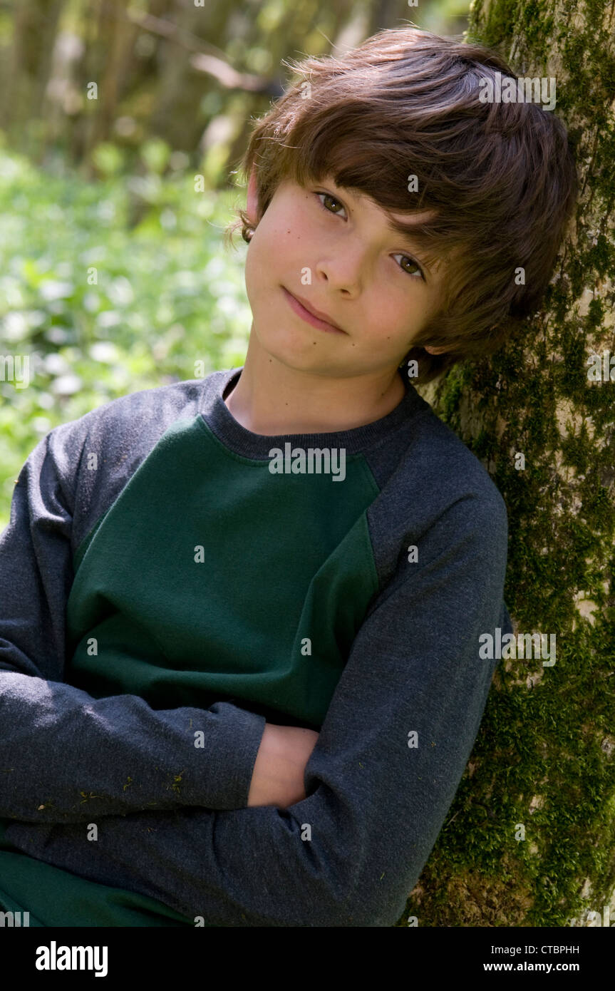 Portrait of a young boy leaning against a tree in woodland Stock Photo ...