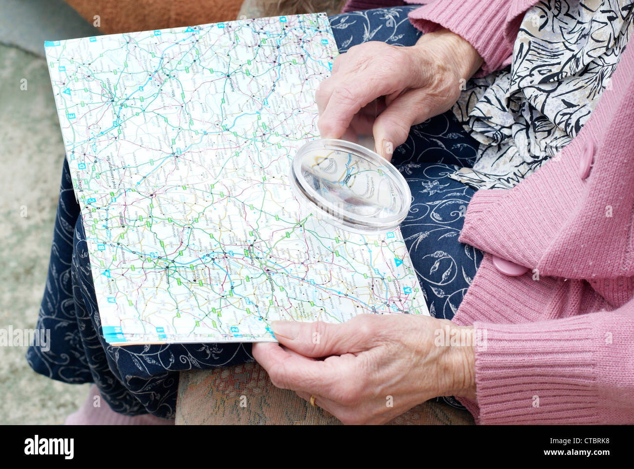 Elderly woman looking at a traditional paper map (maps) of England ...