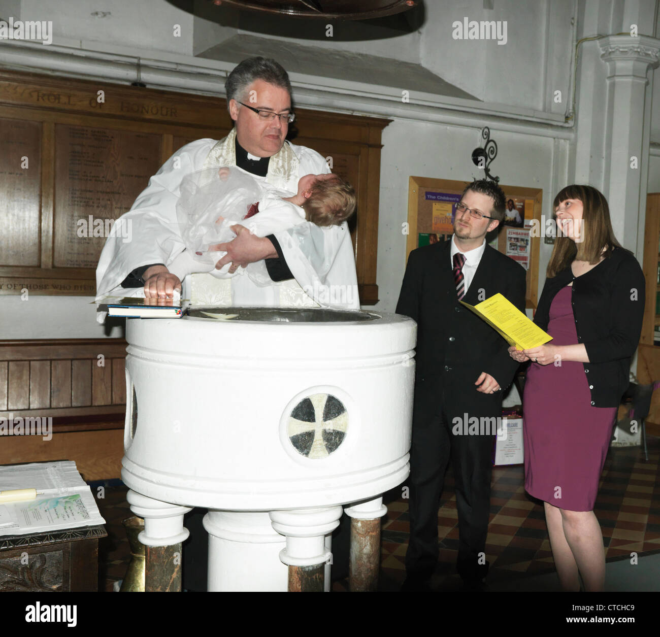 Priest Holding Baby Girl Over Font At With Parents Watching Christening ...