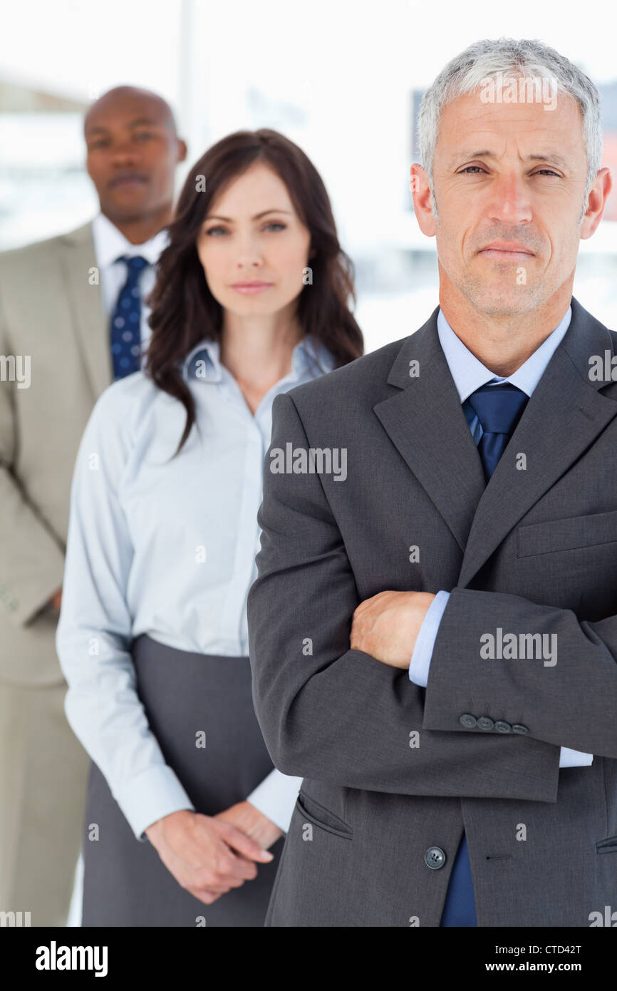 Mature manager crossing his arms seriously in front of two members of ...