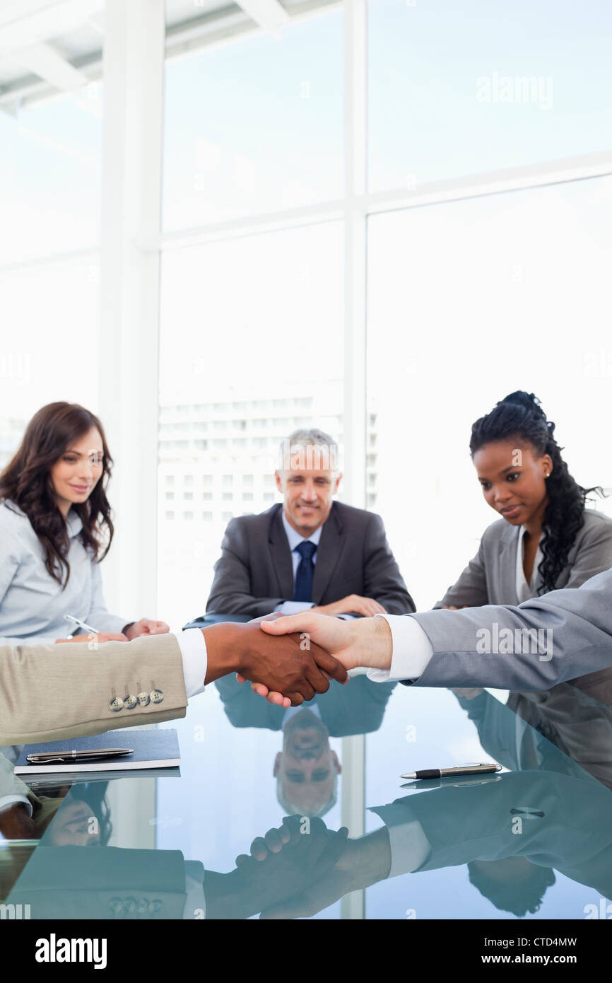 Handshake between two co-workers while their colleagues are looking at ...