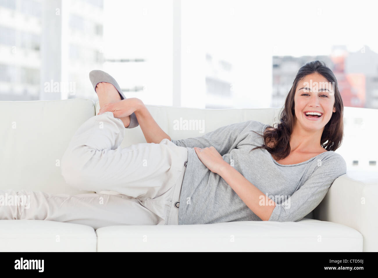 Portrait of a laughing brunette stretching on her sofa Stock Photo - Alamy
