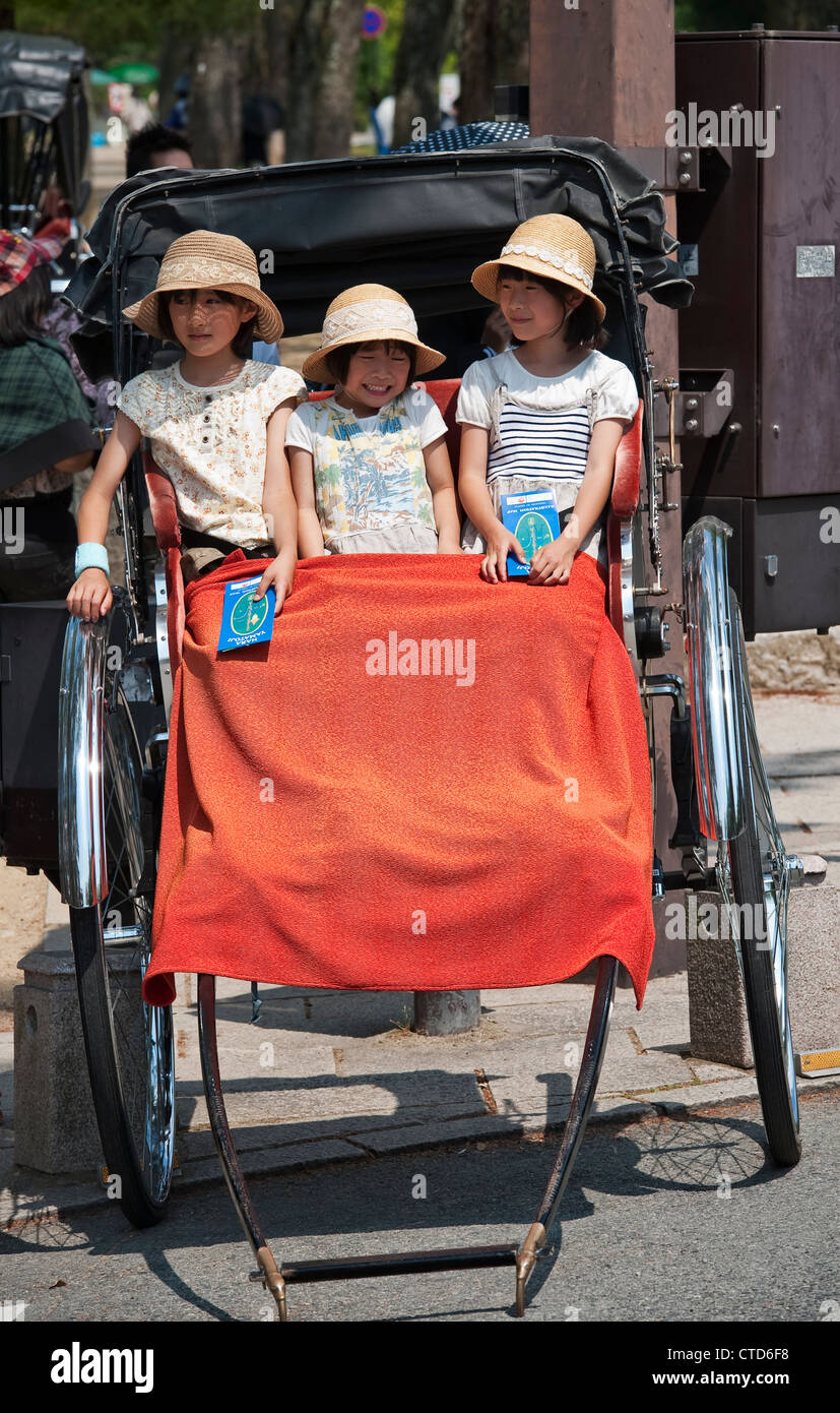 Three young Japanese children wearing straw sun hats and sitting in a ...