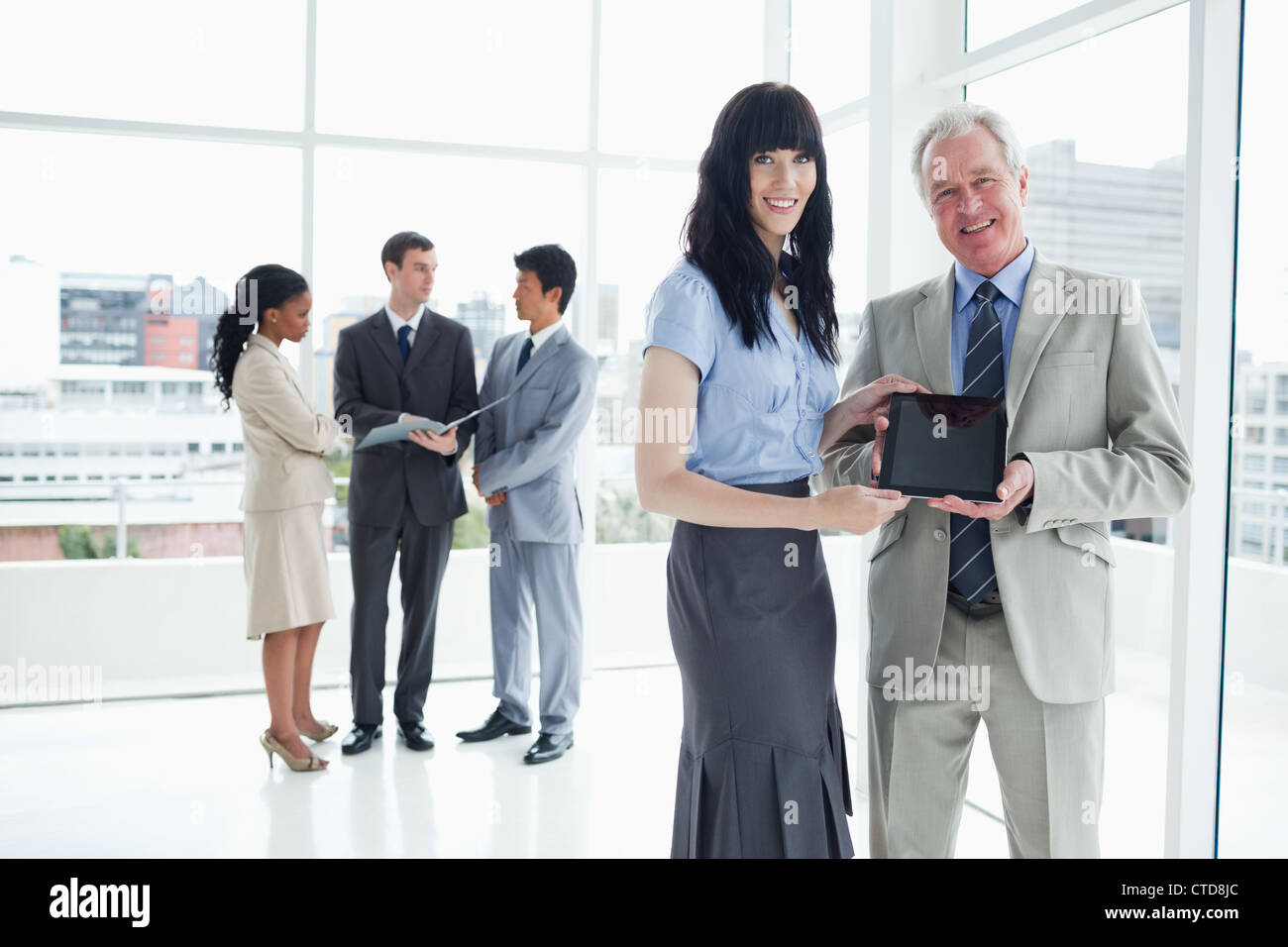 Two smiling business people standing upright showing a tablet computer ...