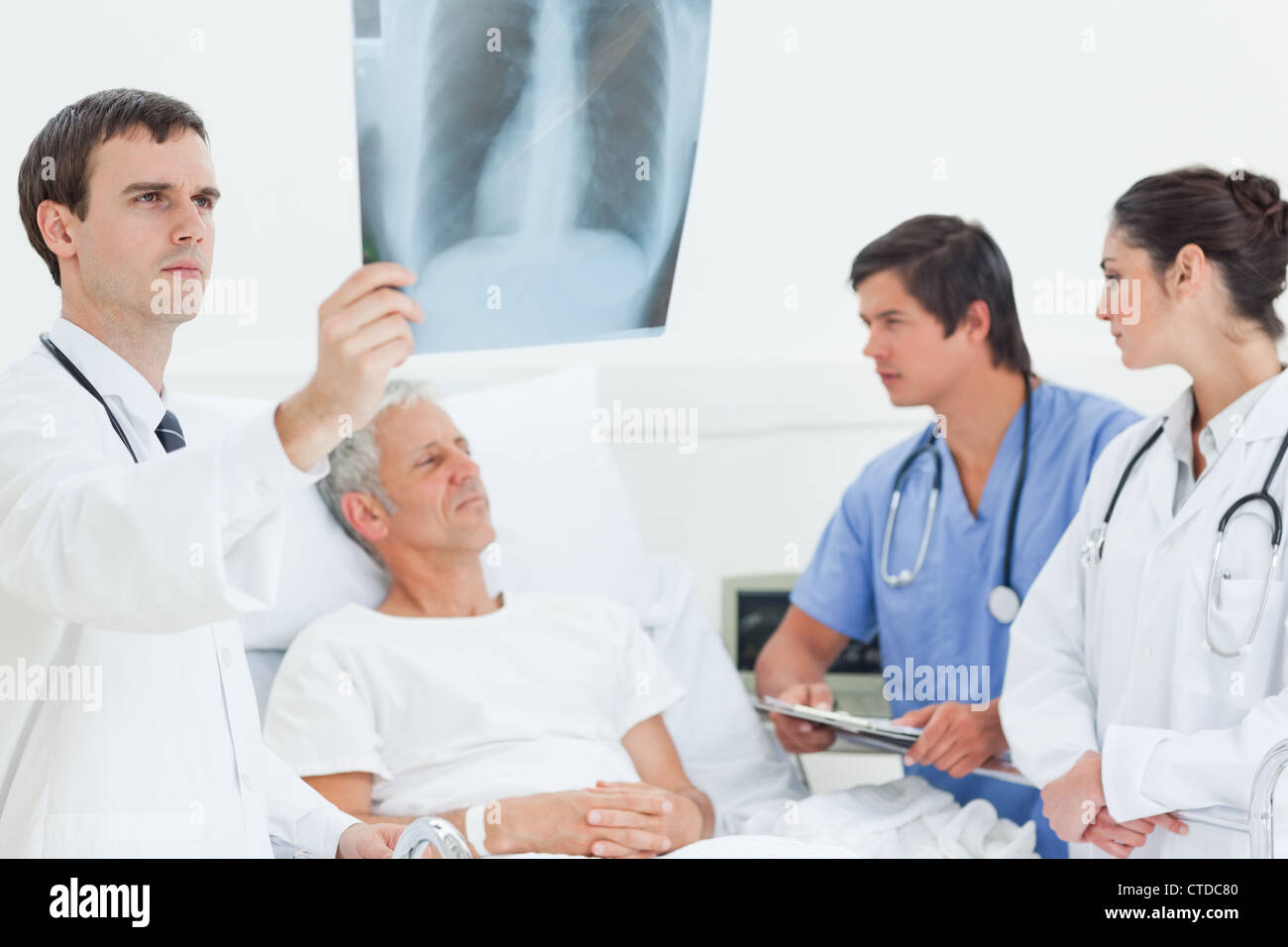Doctor looking at an x-ray scan while standing next to a patients bed ...