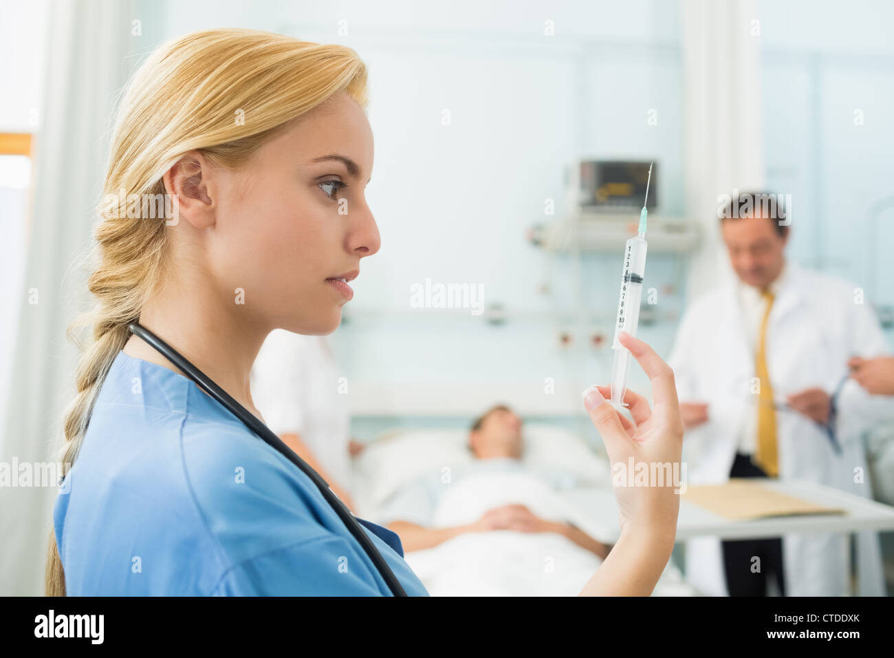 Blonde nurse looking at a syringe while holding it Stock Photo - Alamy