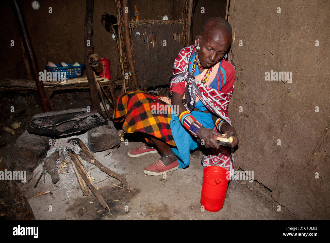 Masai wife of elder chief in traditional costume cooking in her hut in ...