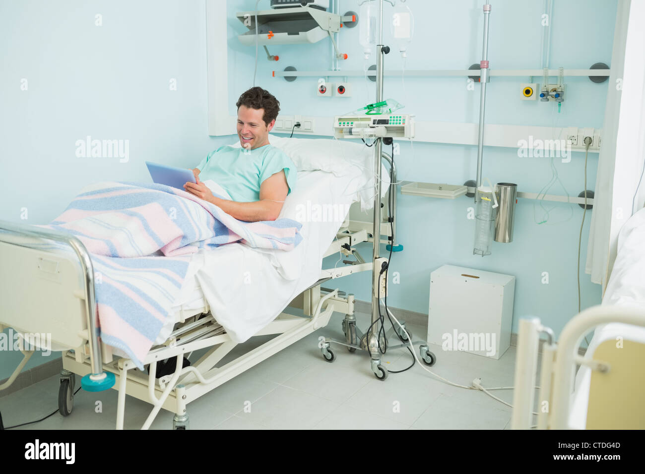 Smiling male patient holding a tactile tablet while lying on a bed ...