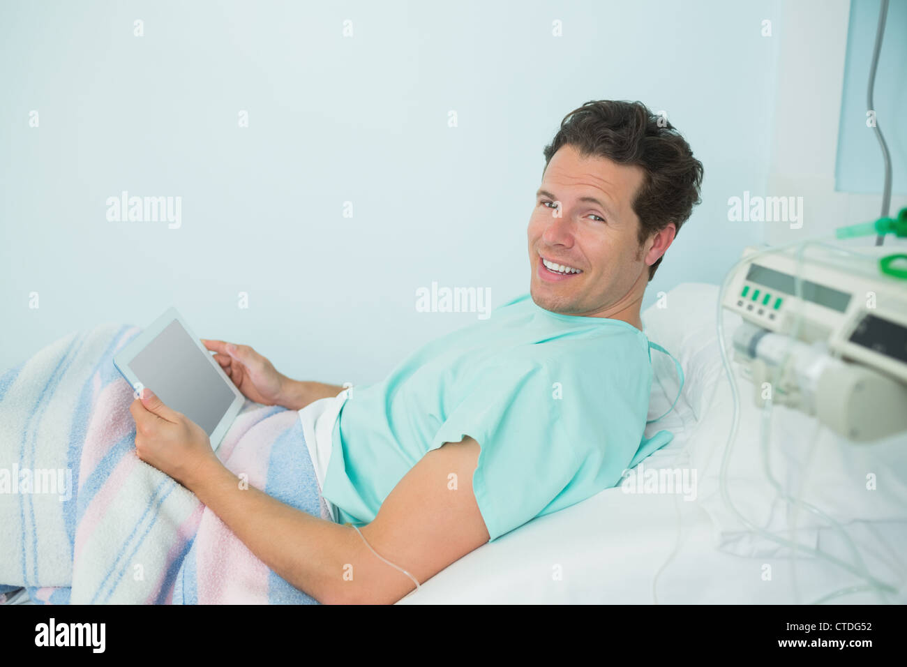 Smiling male patient touching a tactile tablet while lying on a bed ...