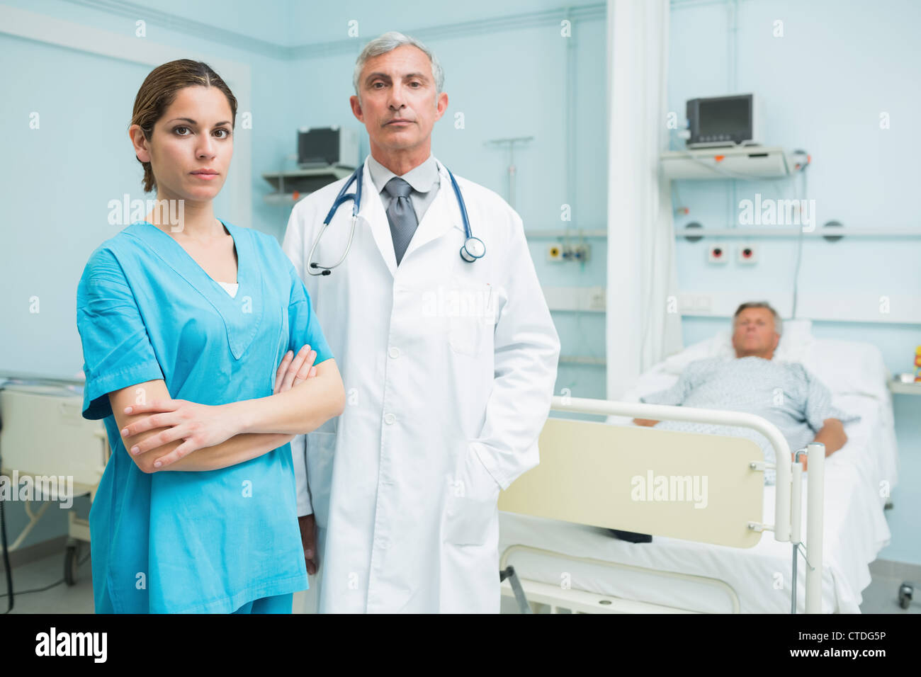 Doctor and nurse with her arms folded standing in the room of a patient ...