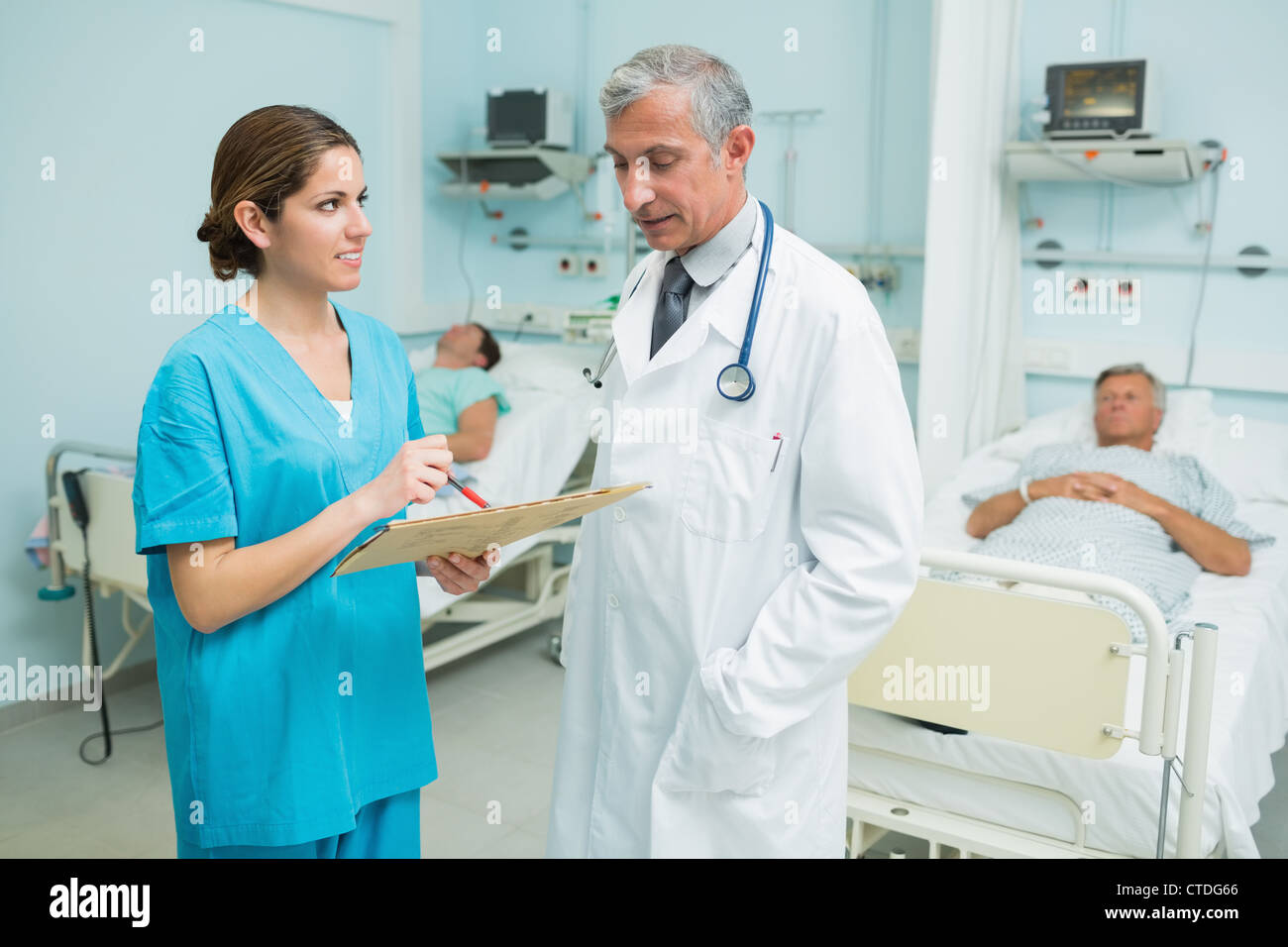 Doctor and a smiling nurse talking in a hospital with two patients ...