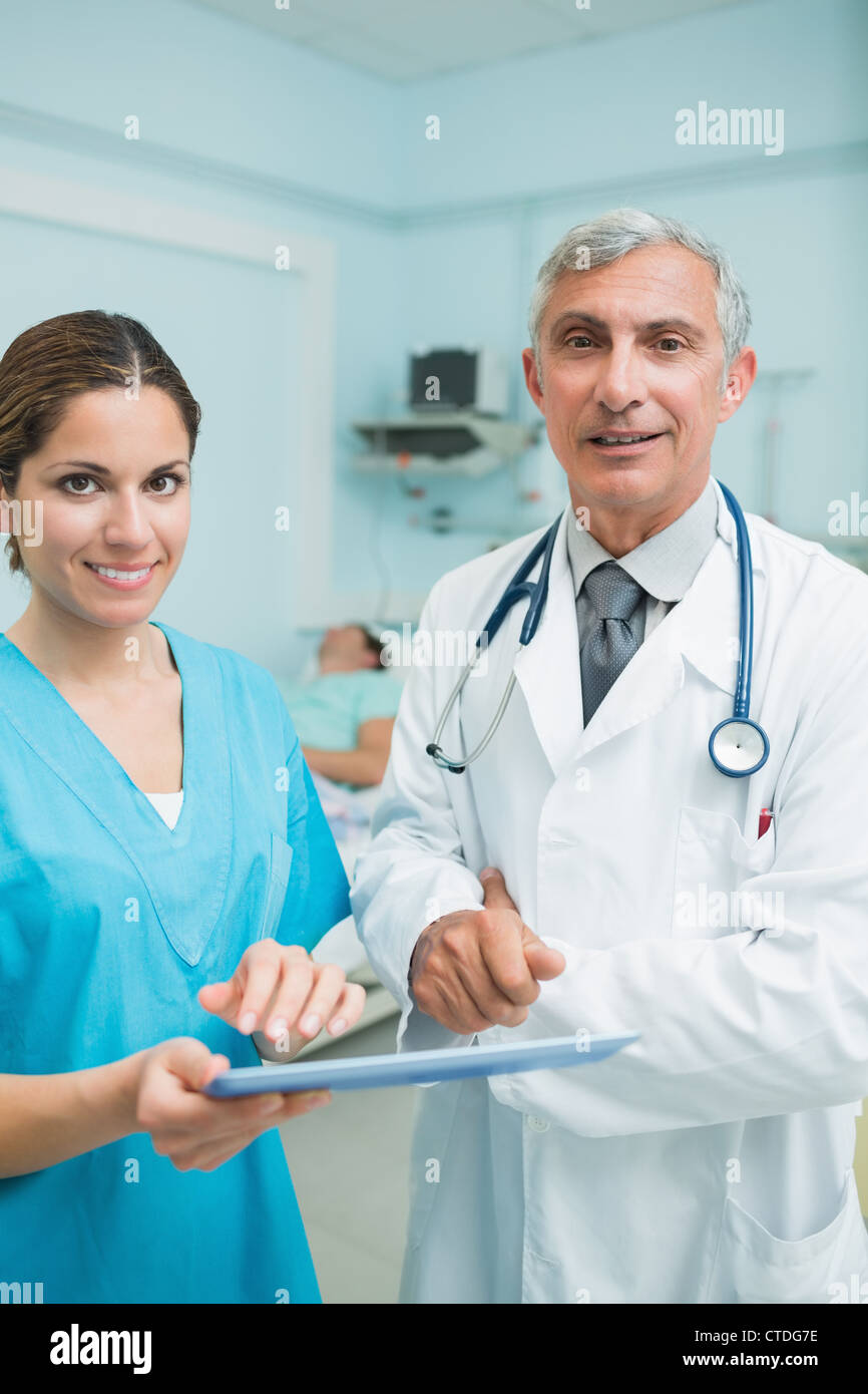 Smiling nurse and a doctor touching a tactile tablet in a hospital with ...