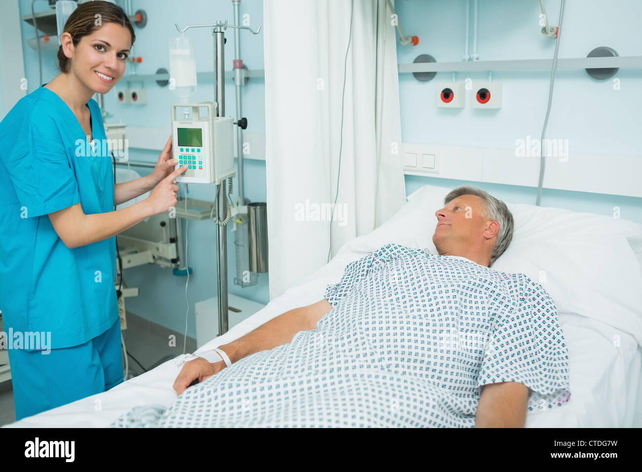 Smiling nurse checking a medical machine next to a patient lying on a ...