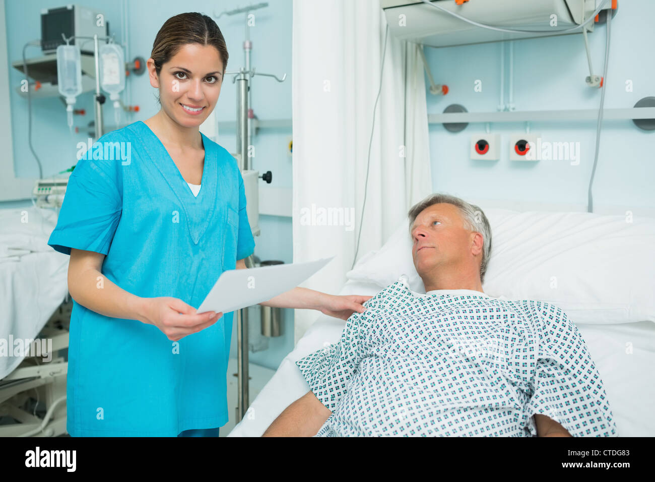 Smiling nurse touching the shoulder of a patient lying on a bed while ...