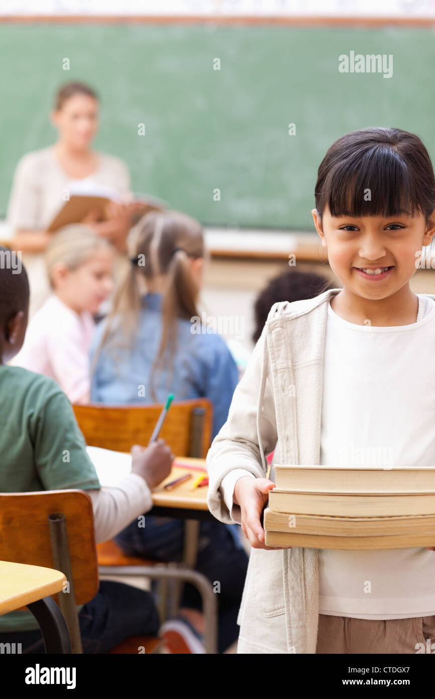Smiling student with pile of books standing in classroom Stock Photo ...
