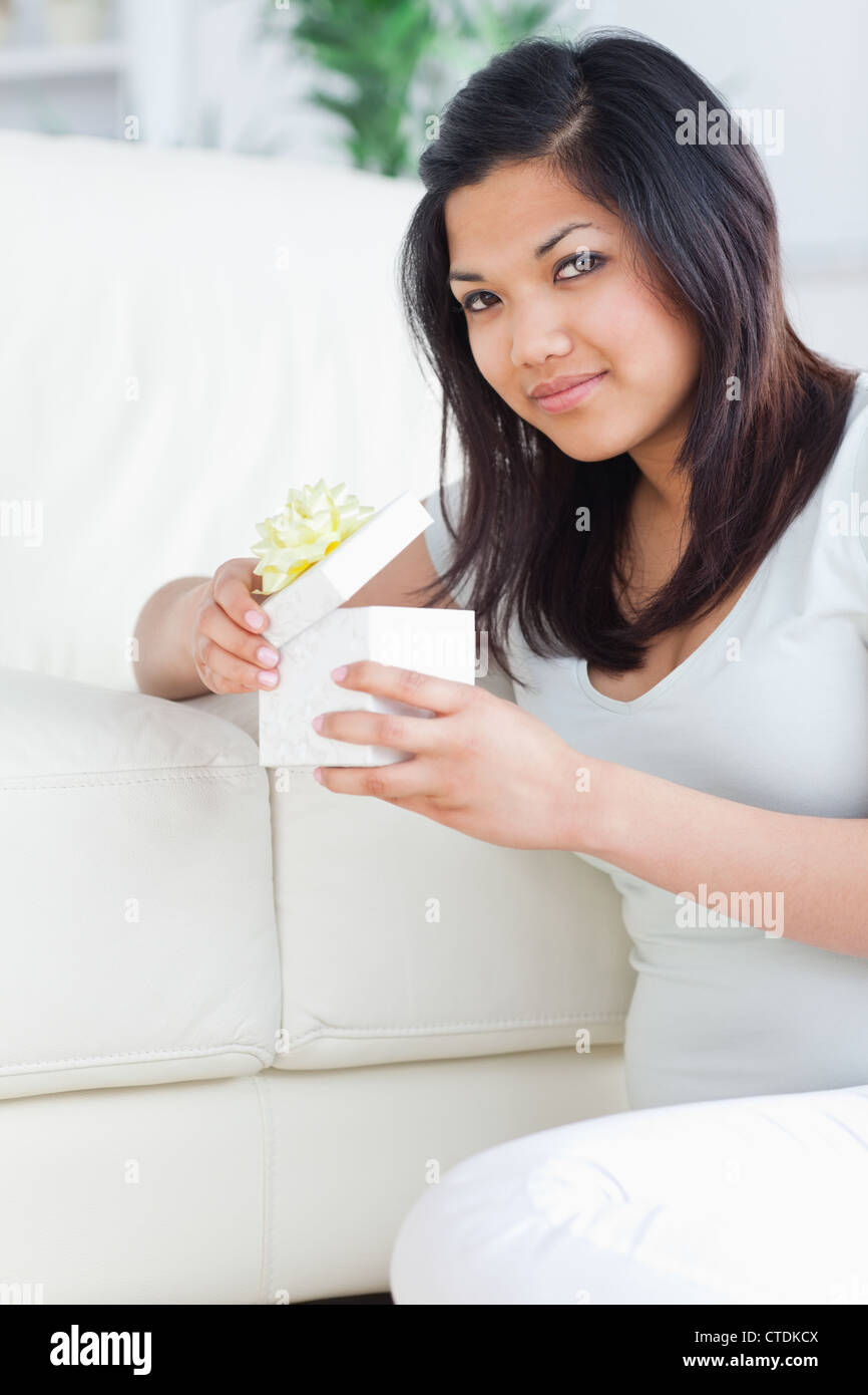Woman opening a gift box while sitting on the floor in front of a couch ...