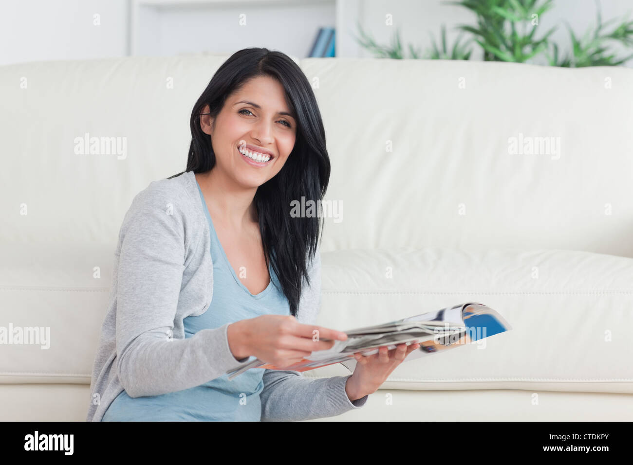 Smiling woman holding a magazine while leaning on a couch Stock Photo ...