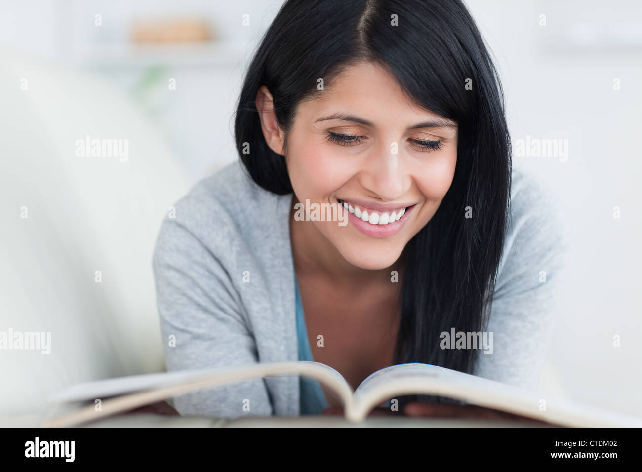 Woman reading a book and smiles as she lies on a couch Stock Photo - Alamy