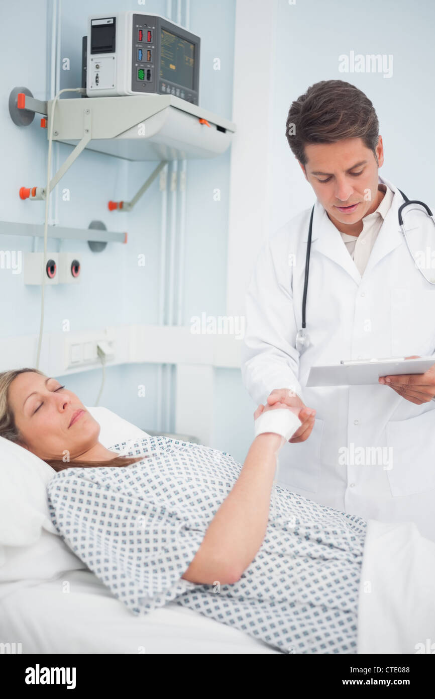 Doctor looking at his chart while holding hand of his patient Stock ...