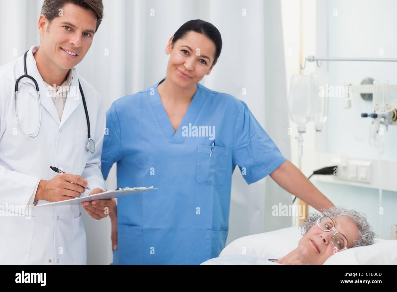 Doctor and nurse looking at camera next to a patient lying Stock Photo ...
