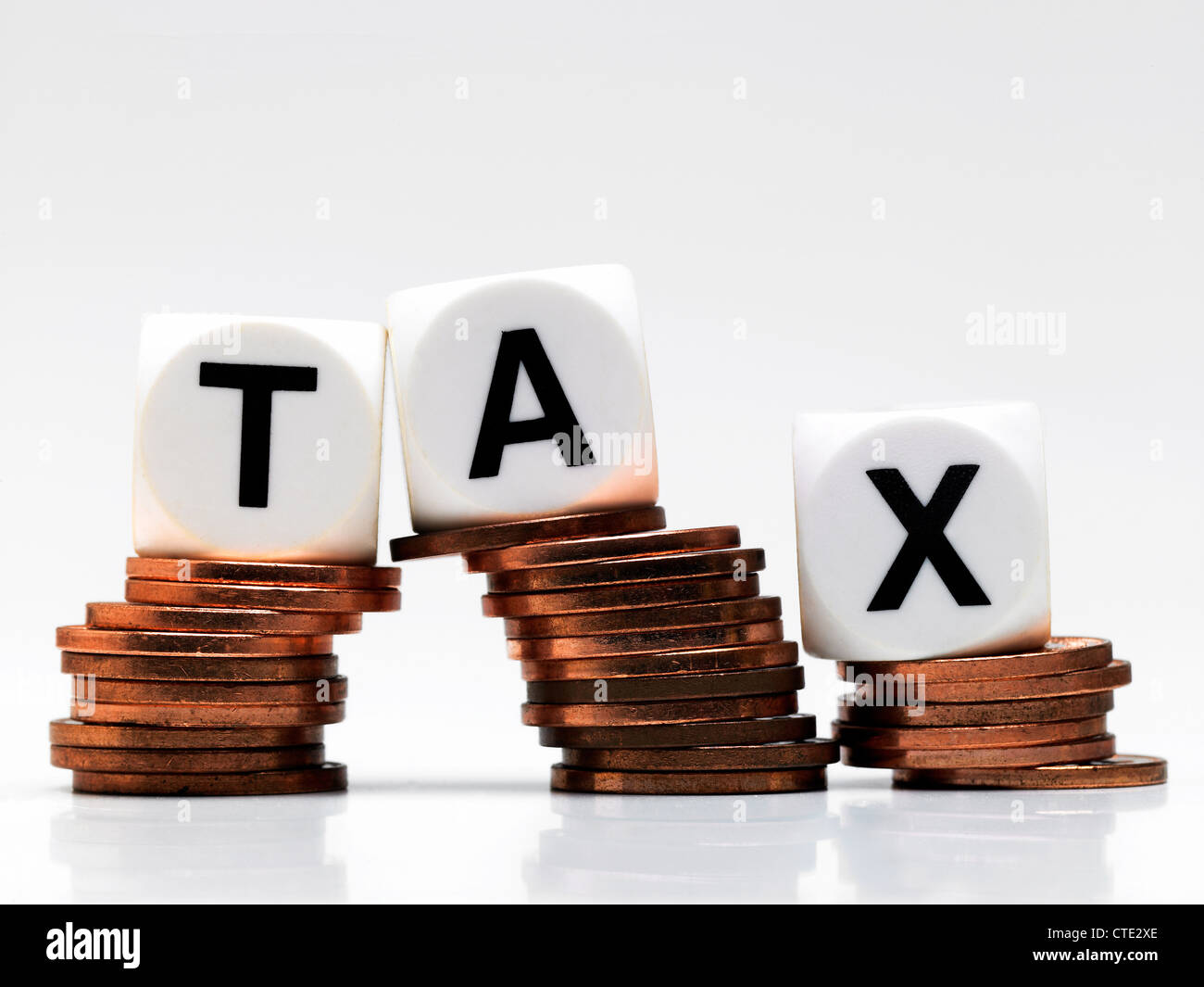 Dice balancing on a pile of coins, spelling out tax Stock Photo - Alamy