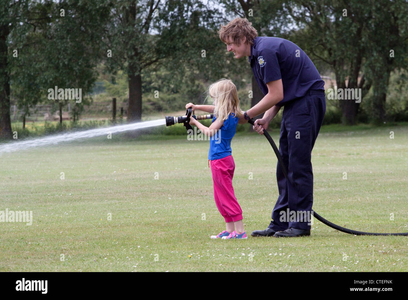 A volunteer fireman helps a small girl hold a fire hose at a family fun ...