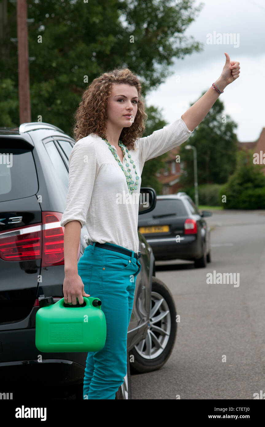 Young female motorist holding a green petrol can and thumbing a lift at ...
