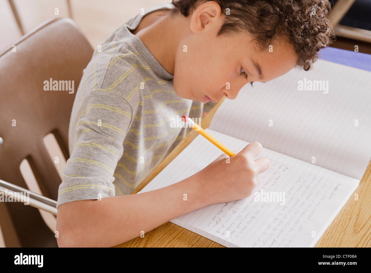 USA, California, Los Angeles, Schoolboy focused on writing in classroom ...