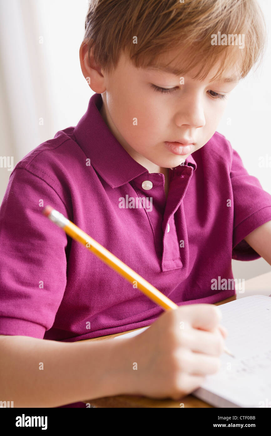 USA, California, Los Angeles, Schoolboy focused on writing in classroom ...
