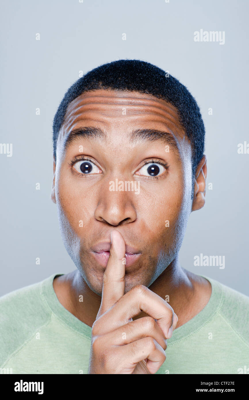 Portrait of young man with finger on his lips, studio shot Stock Photo ...