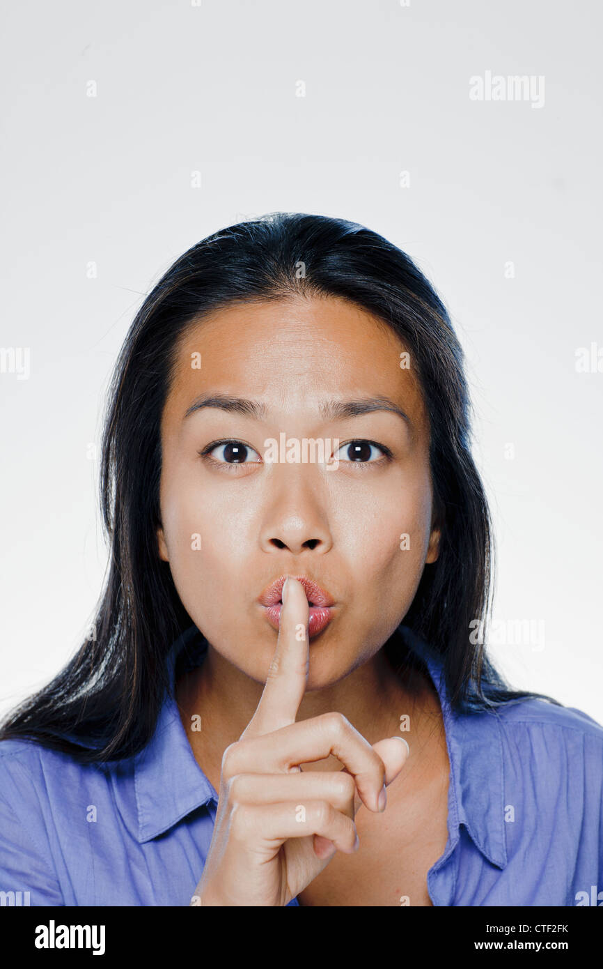 Portrait of young woman with finger on lips, studio shot Stock Photo ...