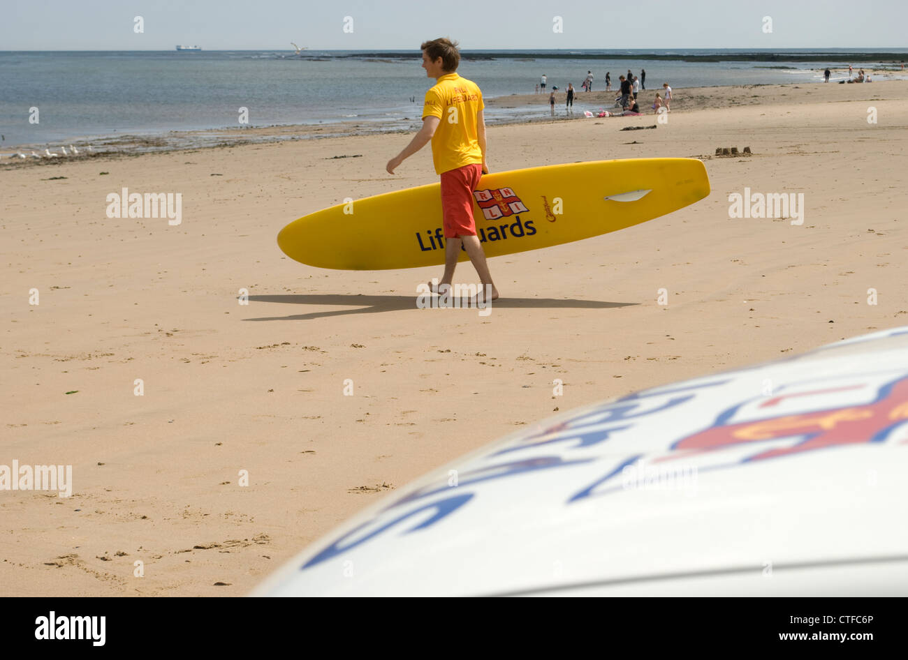 RNLI lifeguard walking towards sea with surf board Stock Photo - Alamy