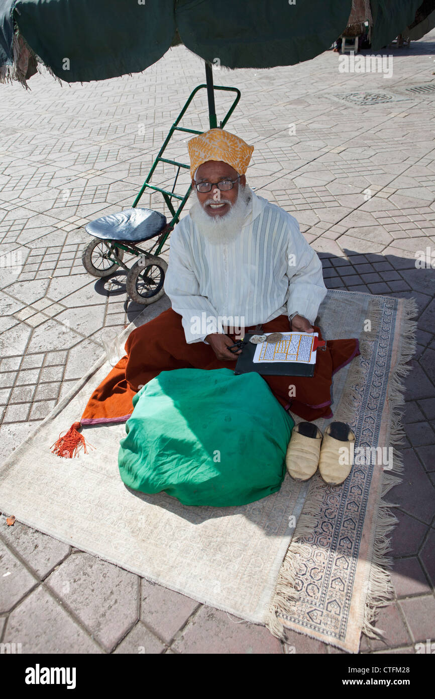 Morocco, Marrakech Square called Djemaa El Fna. Holy man reading from ...