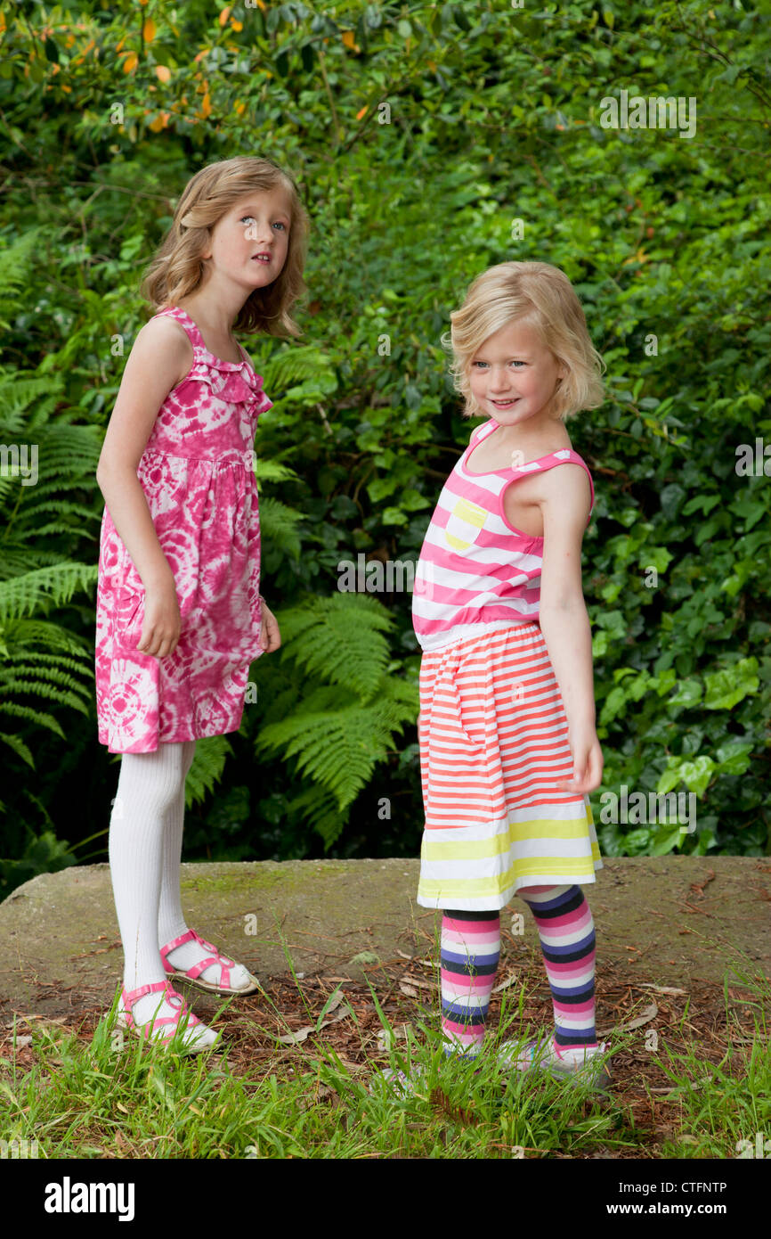 Two sisters are standing outside in front of a green bush Stock Photo ...
