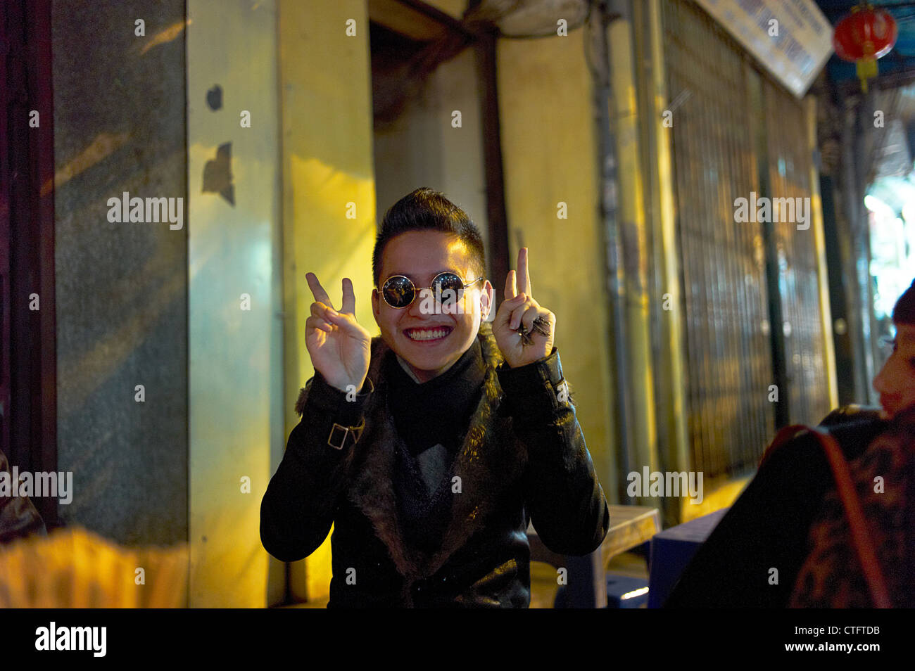 A young man with sunglasses poses with victory signs at an outdoor ...