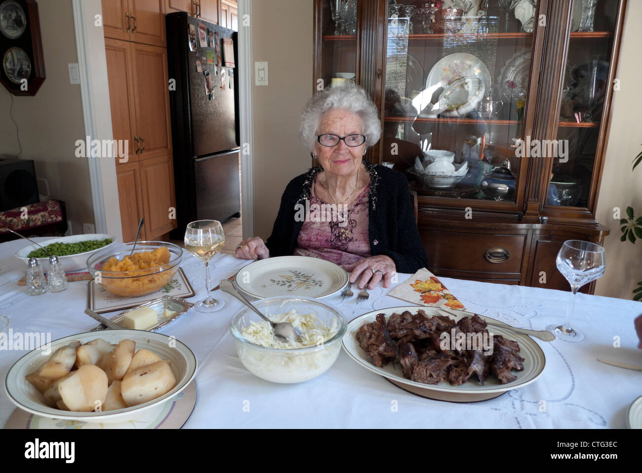 An elderly smiling senior woman sitting at a dining table waiting for ...