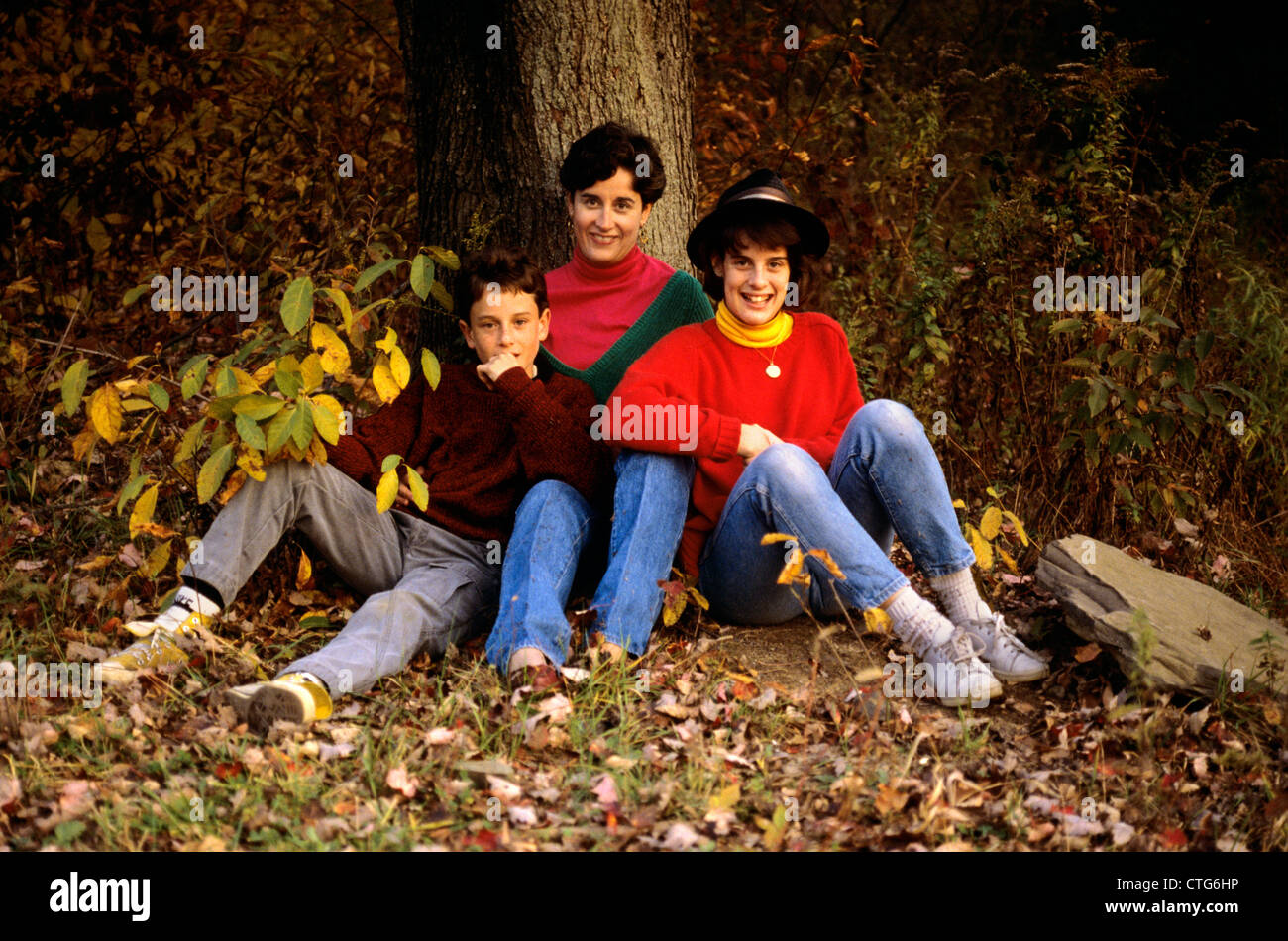 1980s FAMILY MOTHER SON AND DAUGHTER SITTING AT BASE OF TREE IN WOODS ...