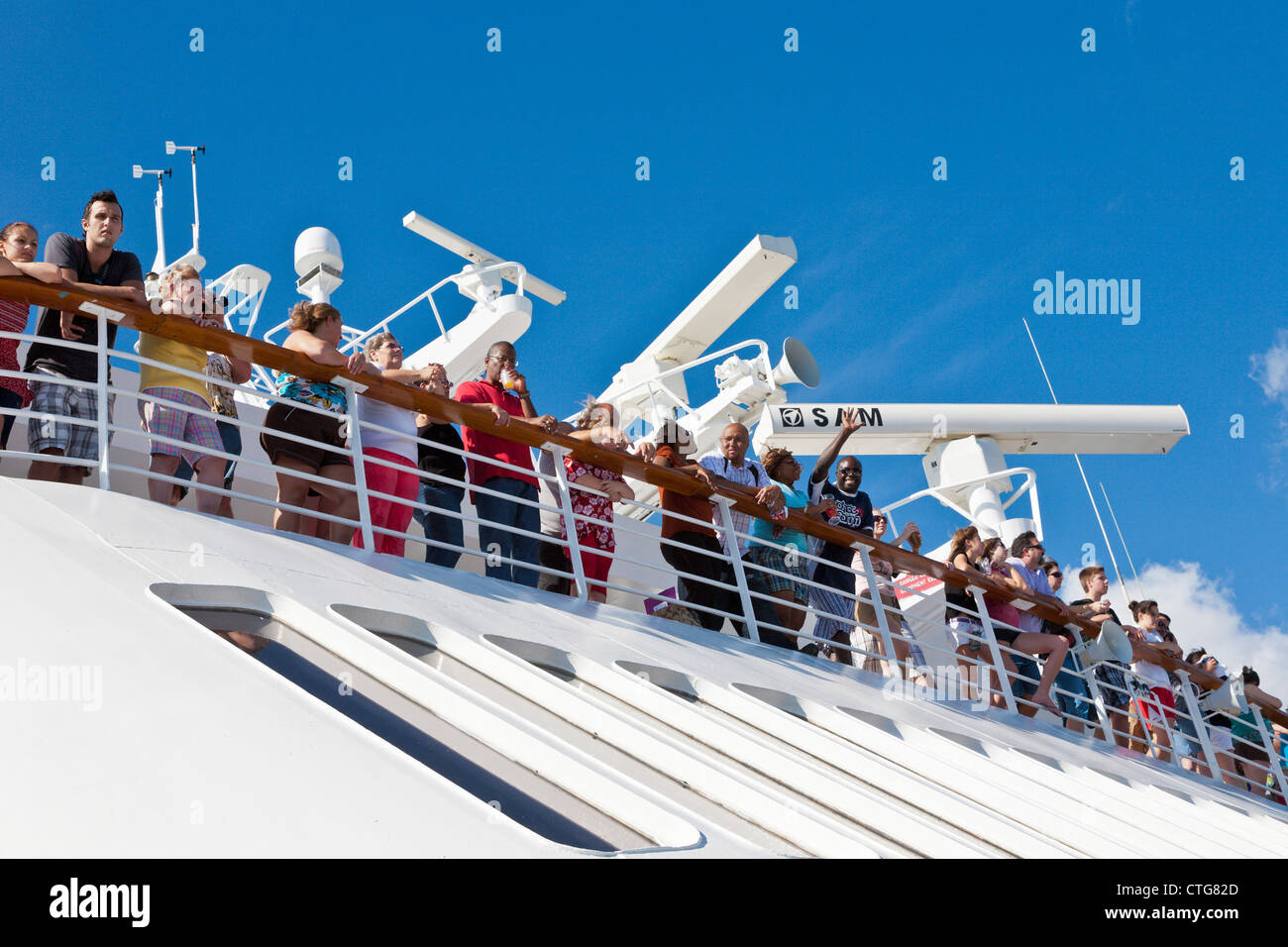 Cruise ship passengers line the rail at the bow of the ship while ...